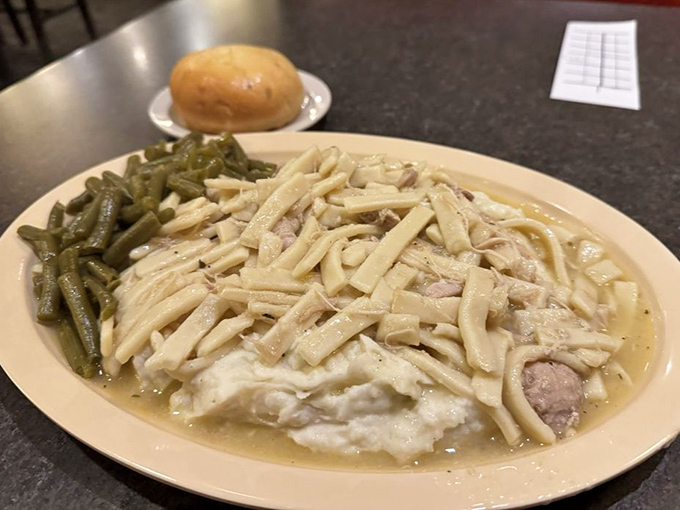 Comfort in a bowl: homemade chicken and noodles swimming in savory gravy alongside green beans, with a dinner roll standing by for essential sauce-sopping duty.