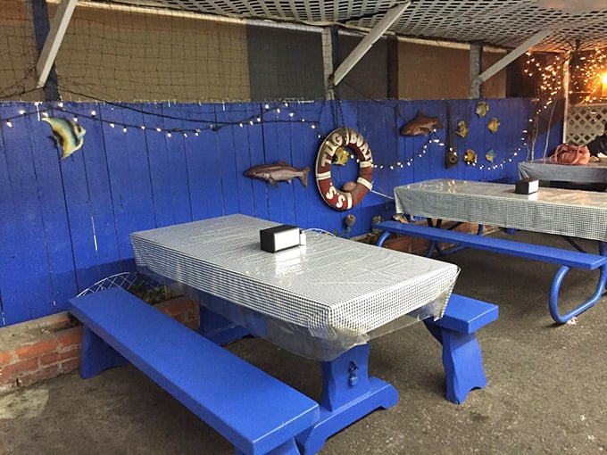 Blue picnic tables under string lights create an outdoor dining space that feels like a casual backyard fish fry—if your backyard had professional fryers.