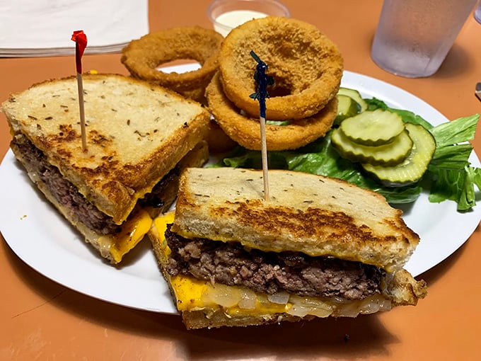 The patty melt – that glorious hybrid of burger and grilled cheese – flanked by golden onion rings that deserve their own fan club.