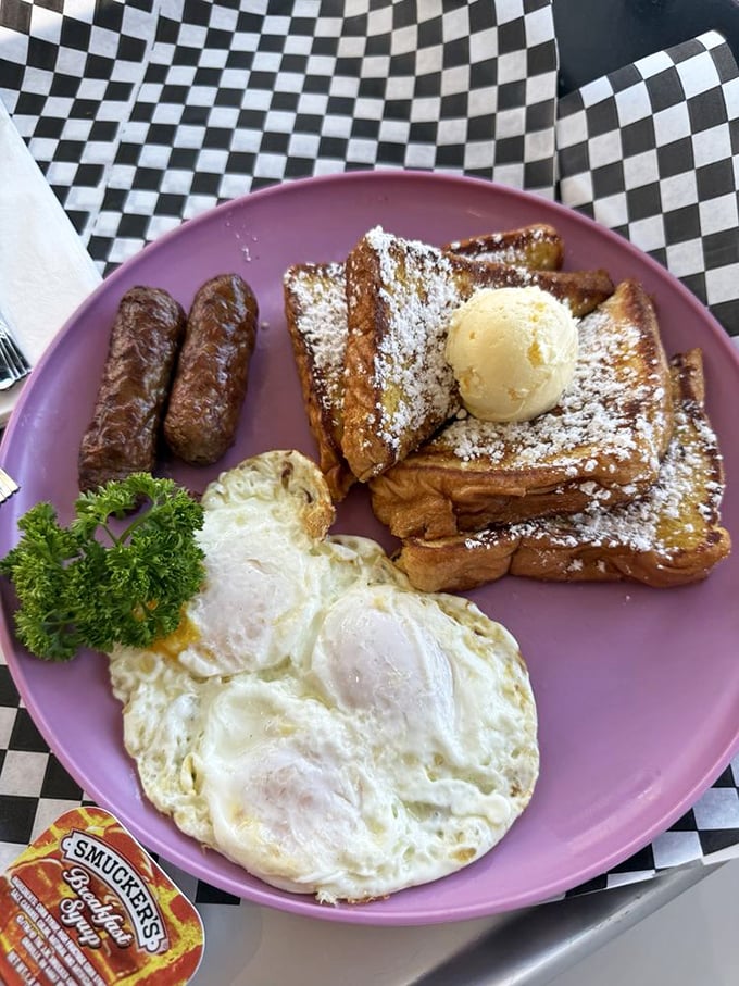 Breakfast perfection on a pink plate—sunny-side eggs, French toast with a powdered sugar snowfall, and sausages standing at attention.