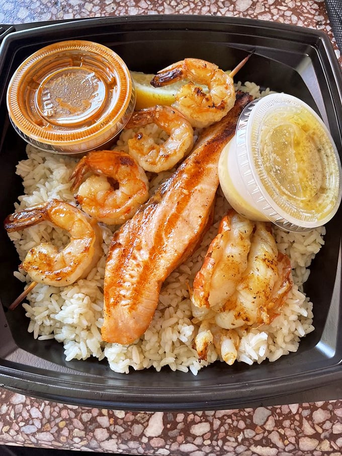 The charbroil sampler—where indecision becomes a virtue. Shrimp and fish living harmoniously on a bed of rice, with sauce cups standing by for optional enhancement.
