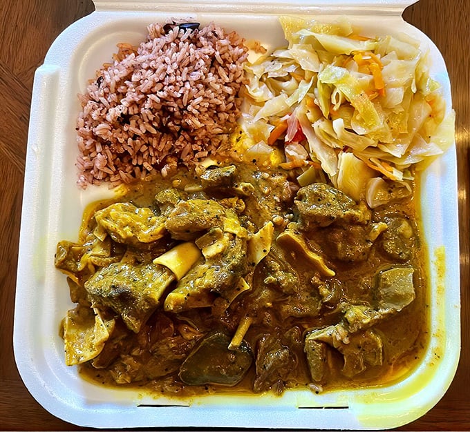Curried goat that doesn't just sit on the plate—it commands attention with its aromatic sauce mingling perfectly with rice and peas.