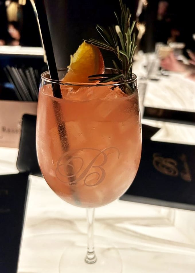 A cocktail garnished with rosemary and citrus—like a sunset in a glass that's dressed for a night at the symphony.
