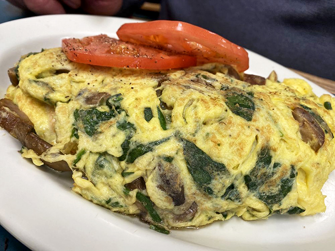 This isn't just an omelet—it's a fluffy yellow canvas painted with mushrooms and spinach, a breakfast masterpiece served with sliced tomato garnish.
