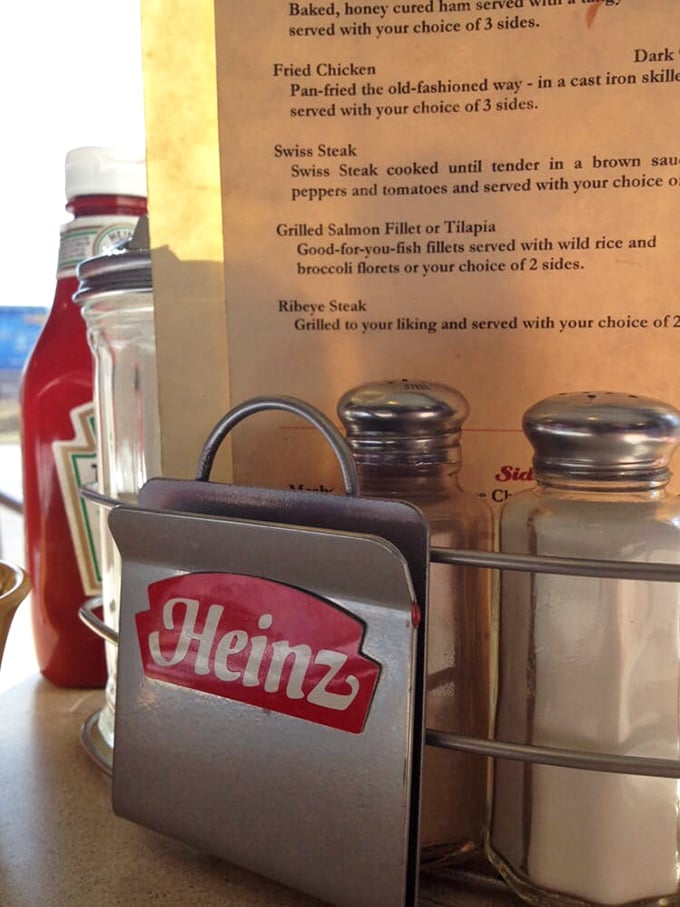 The holy trinity of diner condiments—ketchup, salt, and pepper—standing guard beside a menu that promises fried chicken "pan-fried the old-fashioned way." 