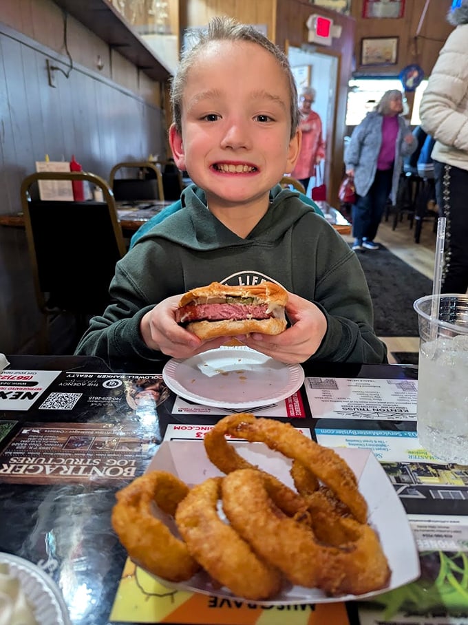 The image shows a young diner enjoying what appears to be the famous bologna sandwich with a side of onion rings – creating food memories that will last a lifetime.