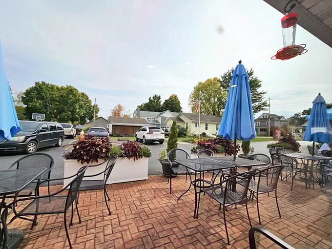 The outdoor patio offers fresh air dining under cheerful blue umbrellas, where flower planters add splashes of color to brick-paved comfort.