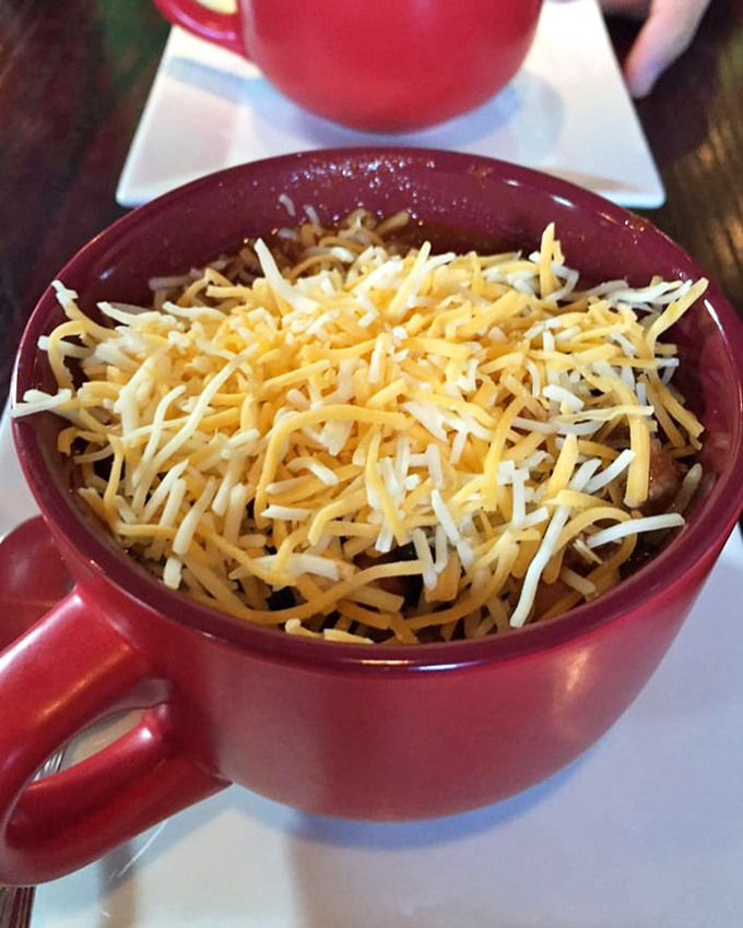 A bowl of chili topped with enough cheese to make Wisconsin proud. This isn't just lunch—it's a warm hug on a cold day, served in a cheerful red mug.