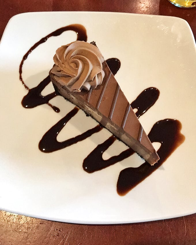 The chocolate cheesecake arrives like the grand finale it deserves to be—rich, velvety, and adorned with artistic drizzles of sauce that make you pause before diving in.