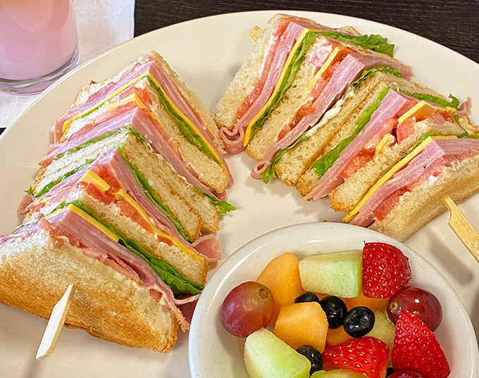 This club sandwich isn't playing games—layers of that famous ham stacked higher than your weekend plans. The fruit cup is just there for moral support.
