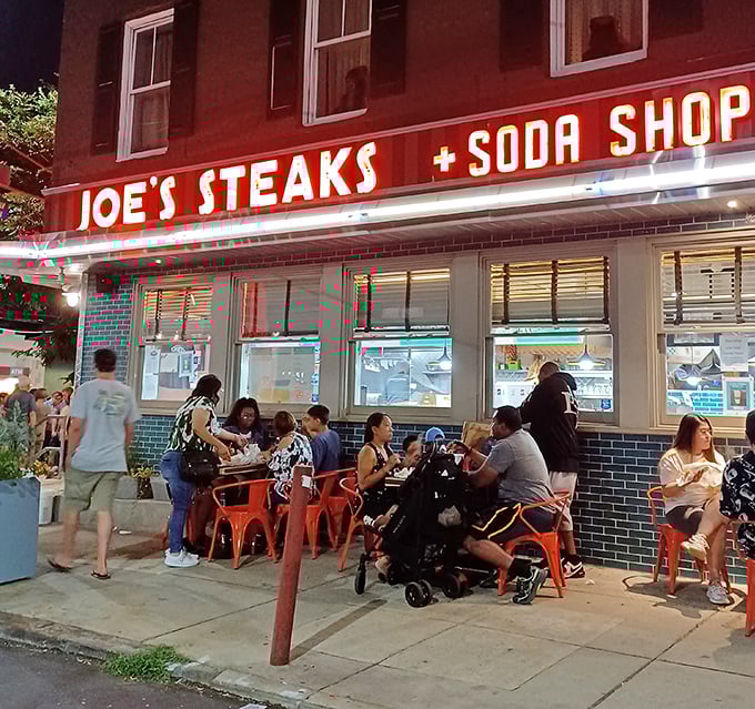 Summer nights at Joe's—where the neon sign serves as both invitation and nightlight for sidewalk diners seeking cheesesteak salvation.