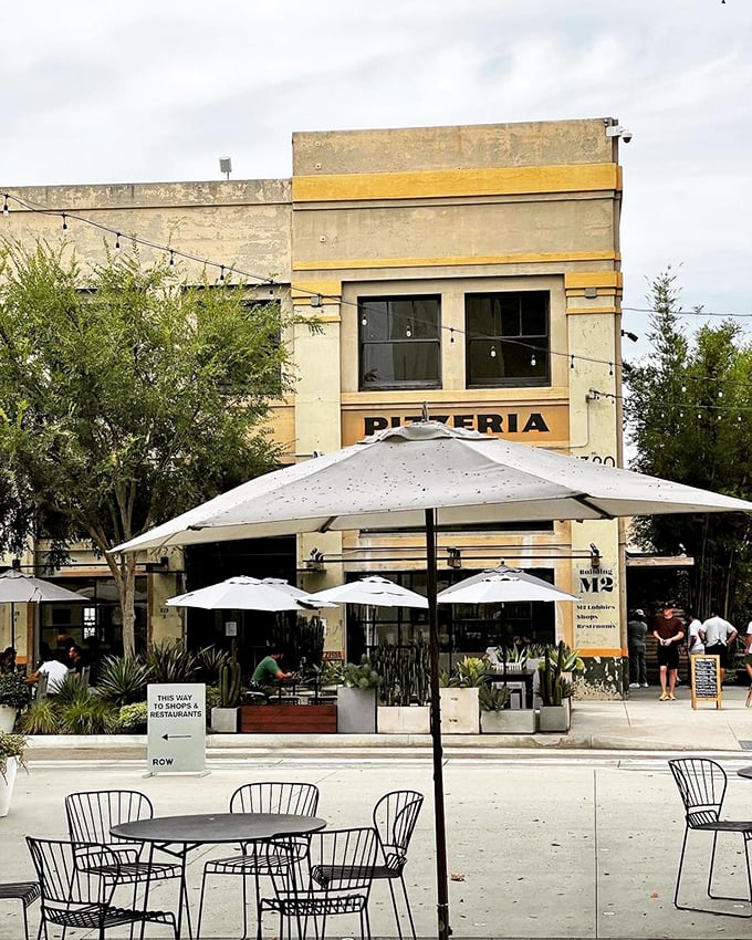 The outdoor seating area beckons like an urban oasis. White umbrellas stand guard over tables where pizza memories are made.
