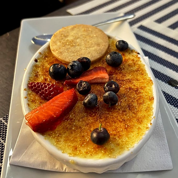 Crème brûlée with a perfectly shattered sugar ceiling, surrounded by berries that look like they're attending a very exclusive dessert gala.