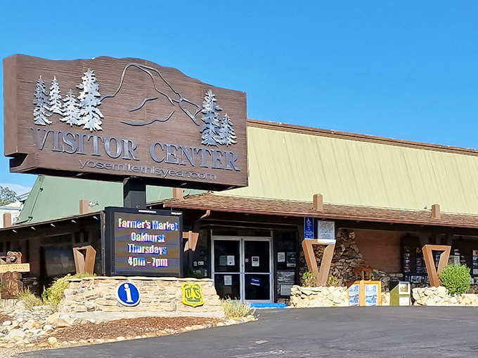 This photo shows the Yosemite Visitor Center in Oakhurst, California, featuring a large wooden sign with a mountain and pine tree design at the entrance.