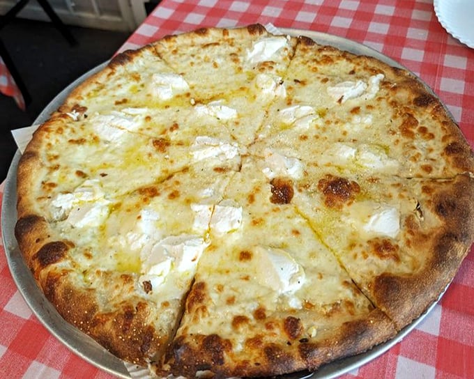The white pizza showcases ricotta's creamy magic – like clouds of dairy goodness that make you forget tomato sauce ever existed. 