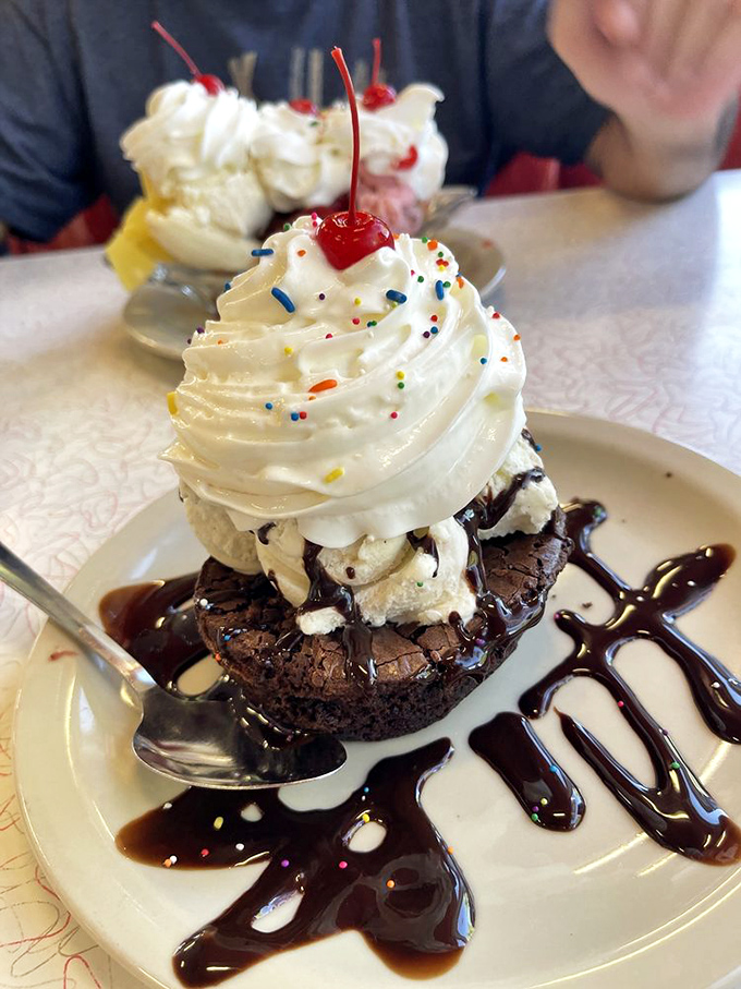 The brownie sundae arrives like a chocolate monument to indulgence, crowned with whipped cream and rainbow sprinkles.