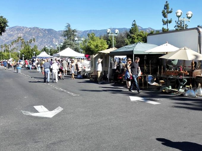 The thrill of the hunt! Shoppers stroll past vendor tents with mountains framing the scene—each step potentially leading to that perfect find.