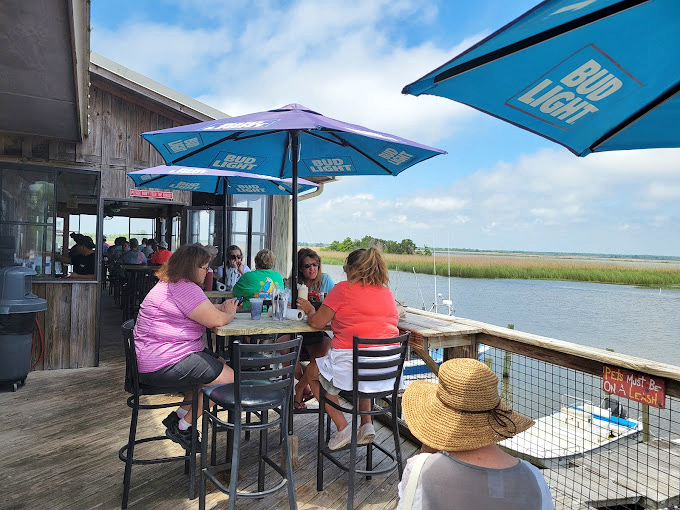 Dining waterside under Bud Light umbrellas with marshland views—proof that the best restaurant patios aren't designed by architects but by nature herself.