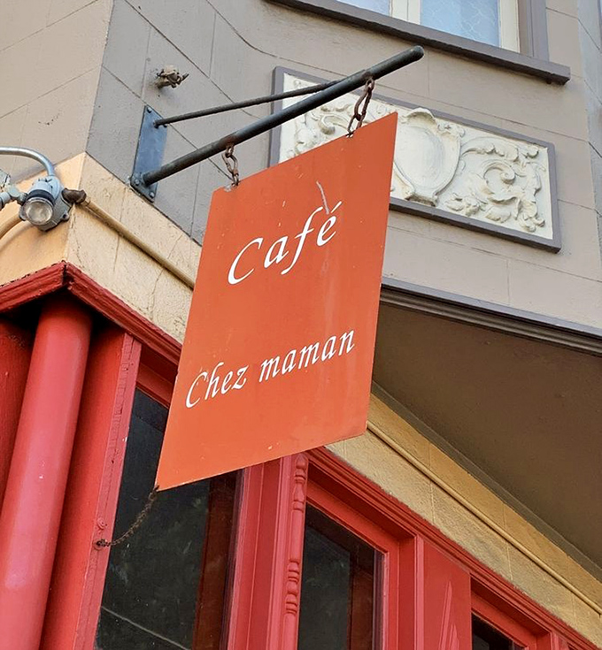 The simple orange sign swinging gently above red trim. "Chez Maman" translates roughly to "You're about to eat really, really well."