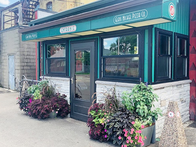 The charming green storefront of Glass Nickel Pizza Co. welcomes you with colorful flower pots – like your favorite neighbor who always has something delicious in the oven.