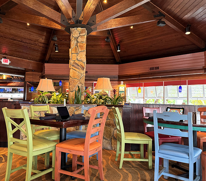 Colorful chairs in lime, coral, and sky blue gather around stone columns beneath soaring wooden ceilings—architecture that whispers "slow down" before you've even ordered.