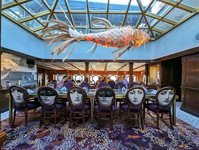 Dining under a sculptural fish mobile while surrounded by chairs featuring artistic faces—this isn't your average seafood joint, it's maritime theater.