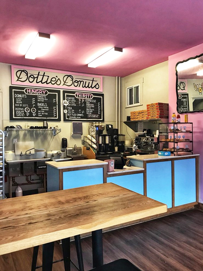 Pink ceiling, wooden countertops, and chalkboard menus create a cozy minimalist space where donuts rightfully remain the star attraction.