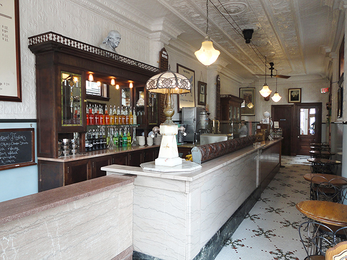 The gleaming marble counter and ornate tin ceiling aren't movie props—they're the real deal. This narrow space somehow holds a century of soda fountain history.