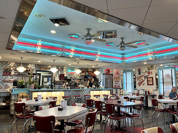 Neon ceiling trim bathes the dining room in a nostalgic glow, while chrome accents and red vinyl chairs complete the authentic mid-century experience.