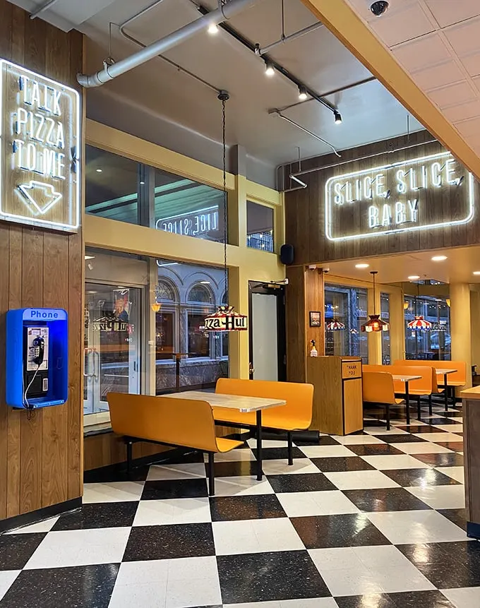 "Slice, Slice, Baby" isn't just clever neon—it's a philosophy. The retro checkered floor and orange booths create pizza's perfect backdrop.