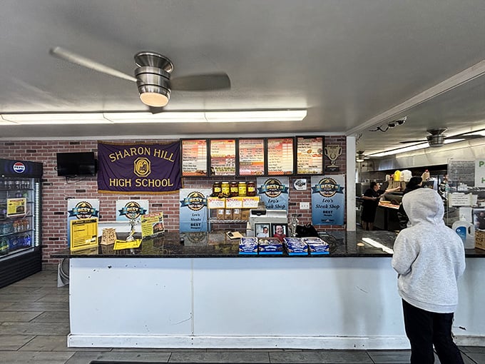 Where local loyalty meets lunchtime legends. The Sharon Hill High School banner watches over countless cheesesteak dreams coming true at the counter.