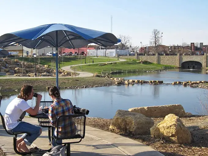 Riverside relaxation at its finest – where college students debate philosophy while ducks conduct their own important meetings.