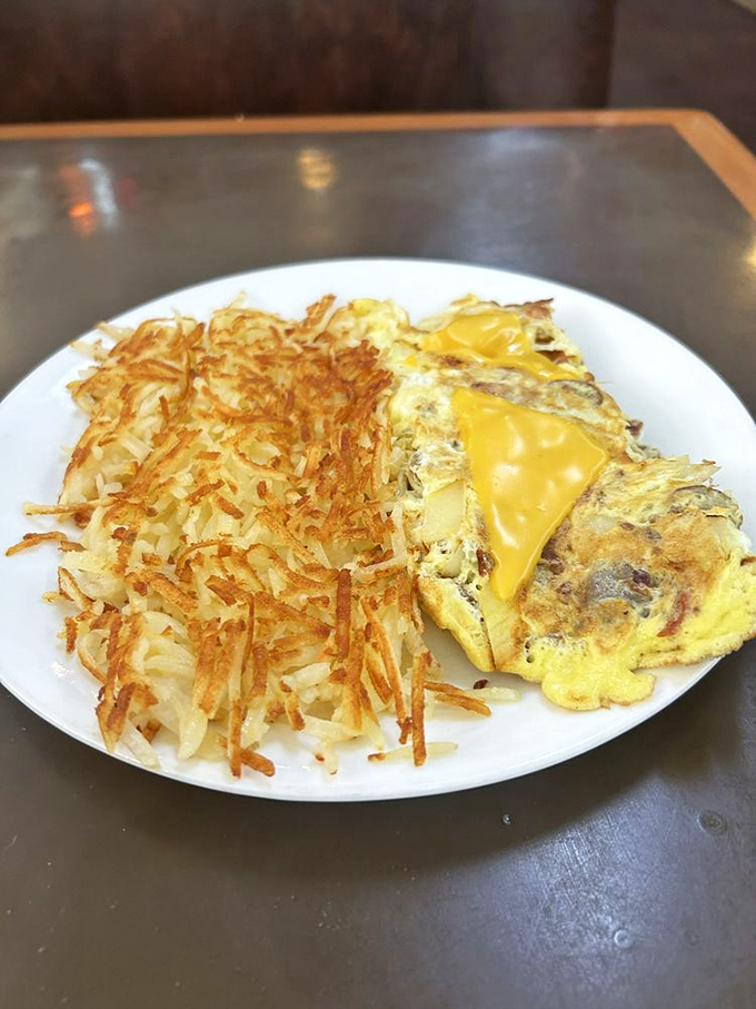 Golden hash browns that crackle with each bite alongside a cheese-laden omelet—this is breakfast architecture at its most magnificent.