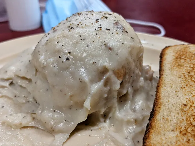 Behold the star attraction: a fluffy buttermilk biscuit swimming in peppery sausage gravy. This isn't just breakfast—it's edible poetry that's worth crossing state lines for.