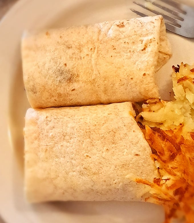 The legendary breakfast burrito – perfectly grilled tortilla hugging fluffy eggs and melted cheese, with crispy hash browns standing guard nearby.