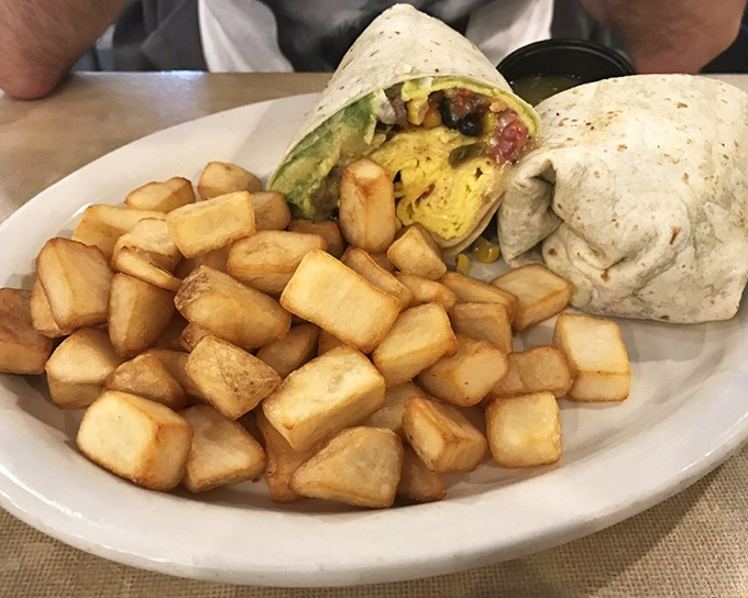 Behold the breakfast burrito in its natural habitat – a tortilla-wrapped miracle flanked by home fries that could make a potato farmer weep with pride. 