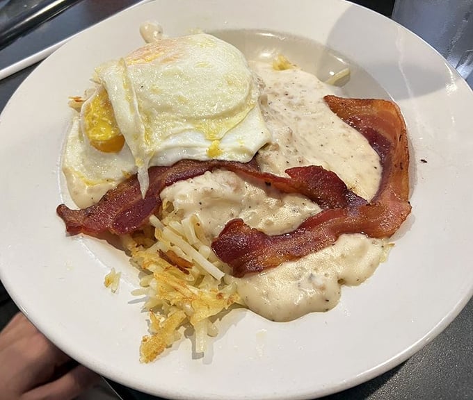 Breakfast architecture at its finest! Layers of hash browns, bacon, and gravy crowned with sunny-side-up eggs—a morning masterpiece that demands respect.