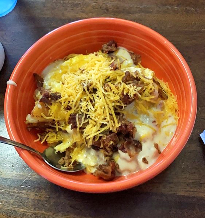 Breakfast alchemy at its finest—potatoes, eggs, meat, and cheese coming together in a vibrant orange bowl to create the ultimate morning fuel.