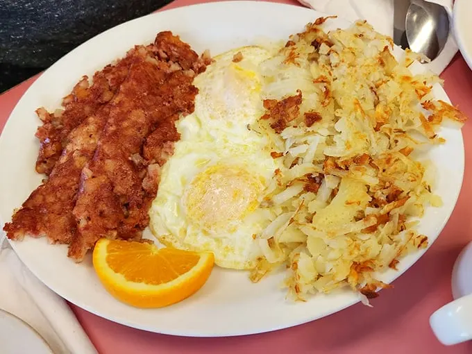Sunny-side up eggs flanked by crispy hash browns and corned beef hash—a breakfast alliance so perfect it deserves its own national holiday.