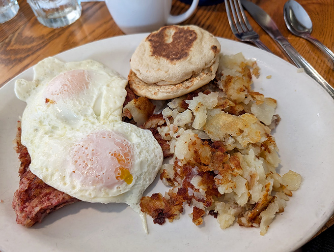 Breakfast perfection on a plate—sunny-side up eggs lounging atop ham steak with crispy hash browns and an English muffin standing by for yolk duty.