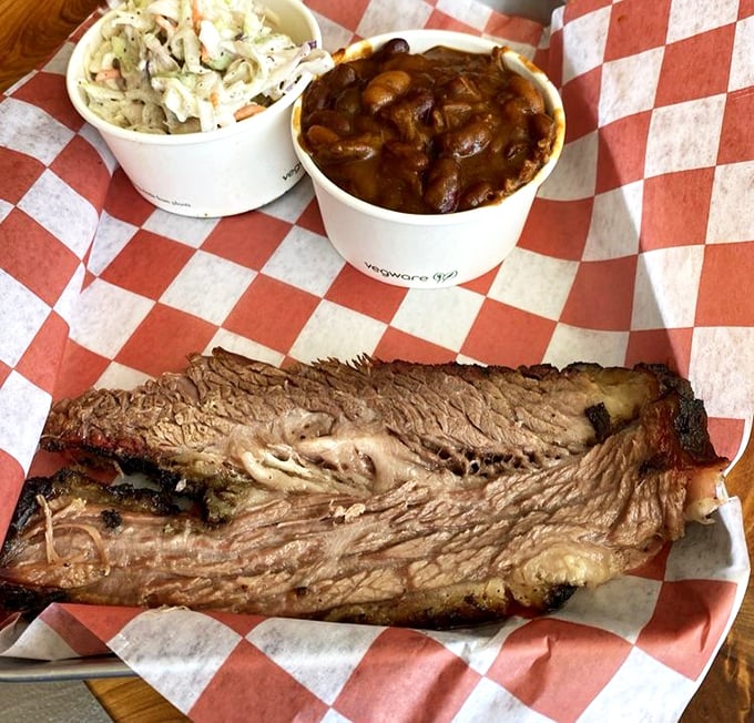 Behold the brisket in all its bark-encrusted glory, resting beside coleslaw and beans like royalty with its loyal subjects.