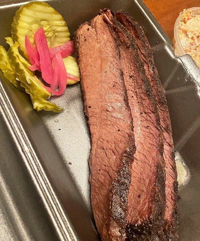 Behold the brisket—pink smoke ring, peppery bark, and that telltale tenderness that speaks of hours in the smoker. Pickles provide the perfect acidic counterpoint.
