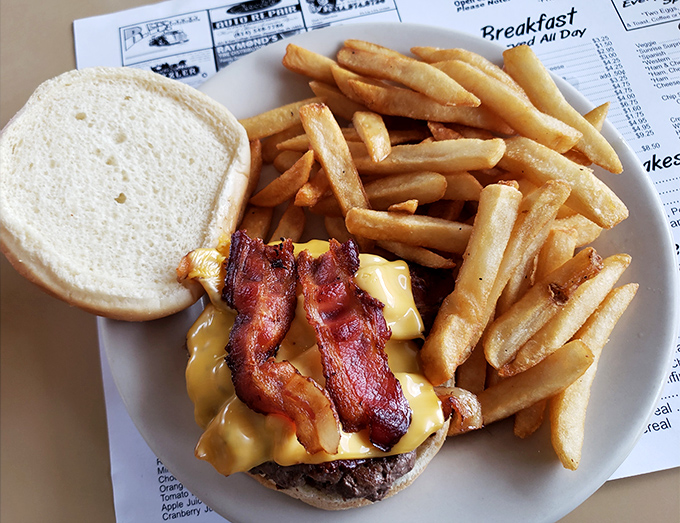 The bacon cheeseburger arrives like a work of art – crispy, glistening bacon draped over melted cheese on a perfectly charred patty.