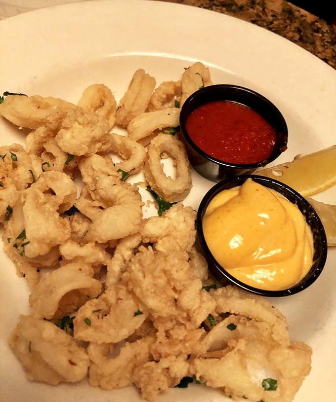 The legendary calamari arrives like a golden crown, perfectly crisp yet tender, with marinara and aioli courtiers standing by.