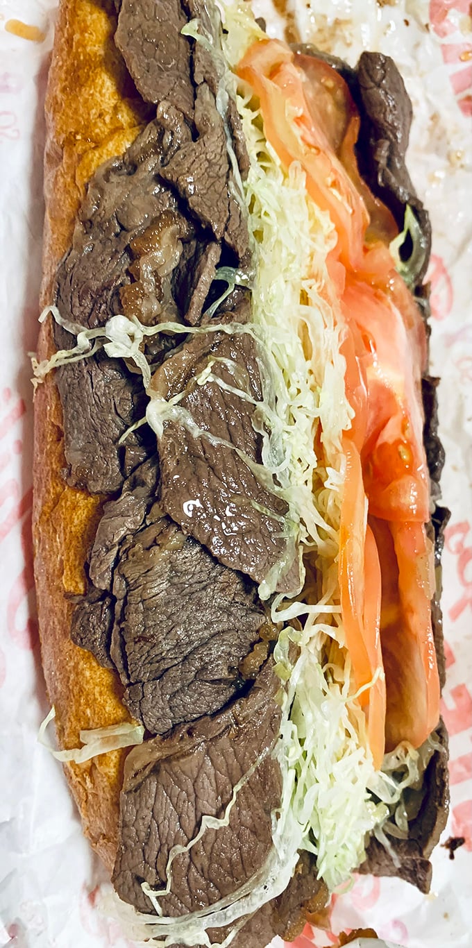 Behold the hybrid masterpiece—thinly sliced steak meets fresh veggies in a textural tango that defines the cheesesteak hoagie experience.