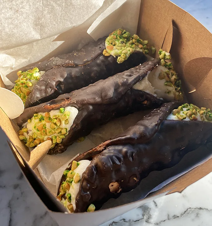 Chocolate-dipped cannoli with pistachio garnish – the dessert equivalent of putting on a tuxedo. One bite and you'll understand why people cross state lines.