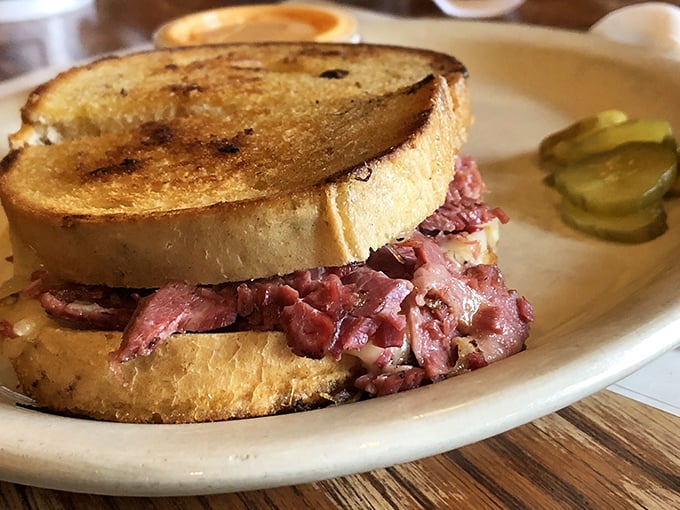 The Reuben sandwich in its natural habitat—a mountain of corned beef nestled between grilled rye, with a pickle standing guard.