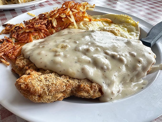 Country fried steak swimming in peppery gravy with crispy hash browns—proof that heaven exists and it's on this plate.