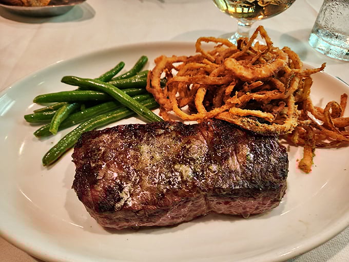 Behold the Delmonico in its natural habitat – perfectly seared, accompanied by crispy onion strings and green beans that actually taste like vegetables should.