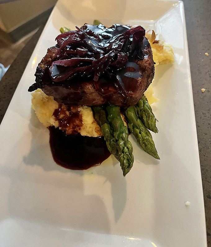 This filet mignon doesn't just sit on the plate—it presides over it, with asparagus soldiers standing at attention and mashed potatoes catching every drop of that glorious sauce.